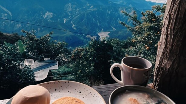 Uma mesa com um prato de comida, uma caneca e vista para uma paisagem montanhosa.