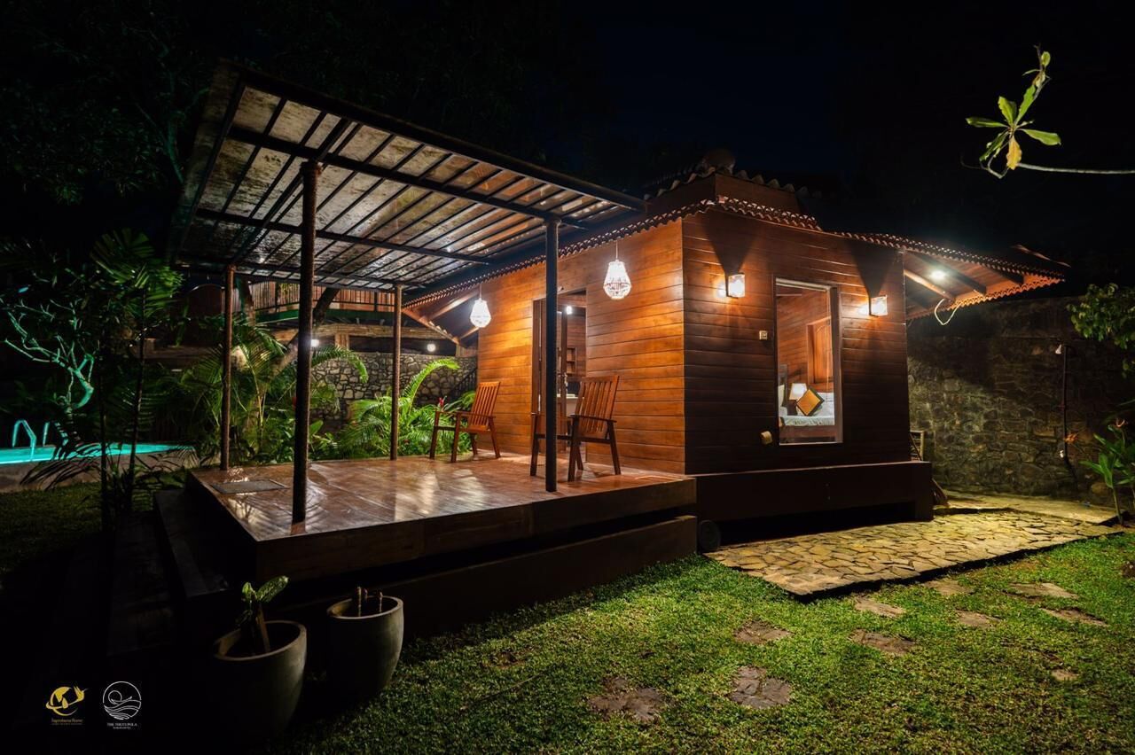 Uma cabana de madeira com alpendre coberto, piscina e caminho de pedra.