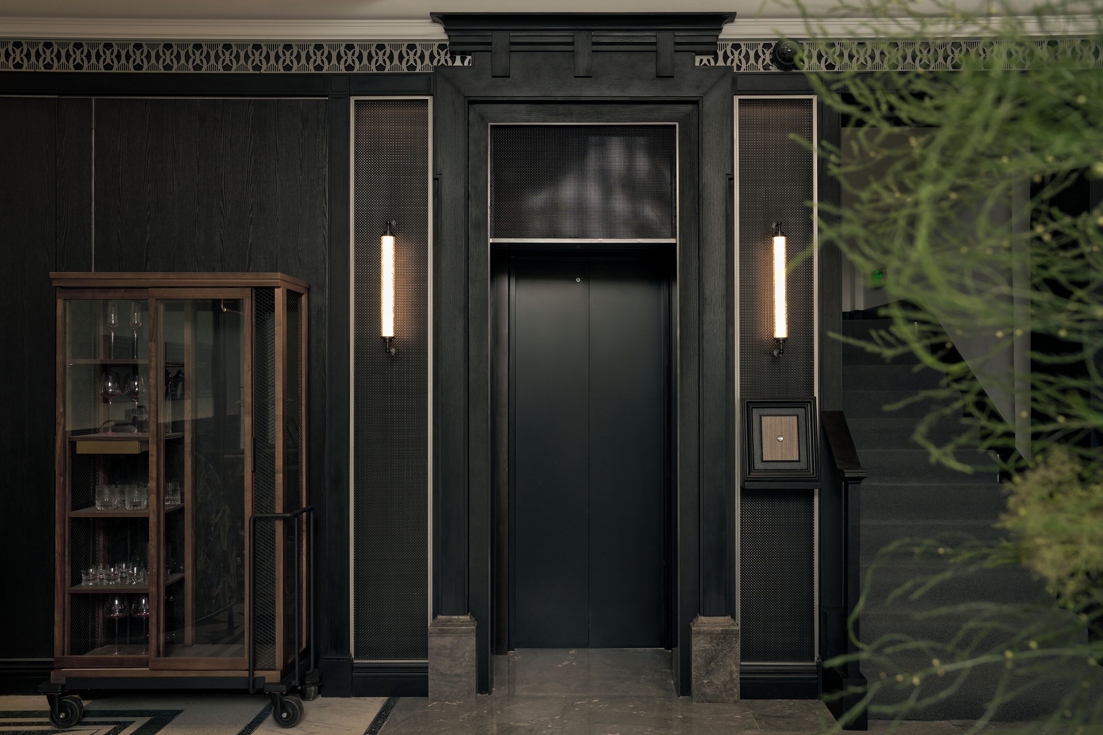 Um elevador de madeira escura com design moderno, ladeado por duas luminárias altas e finas.