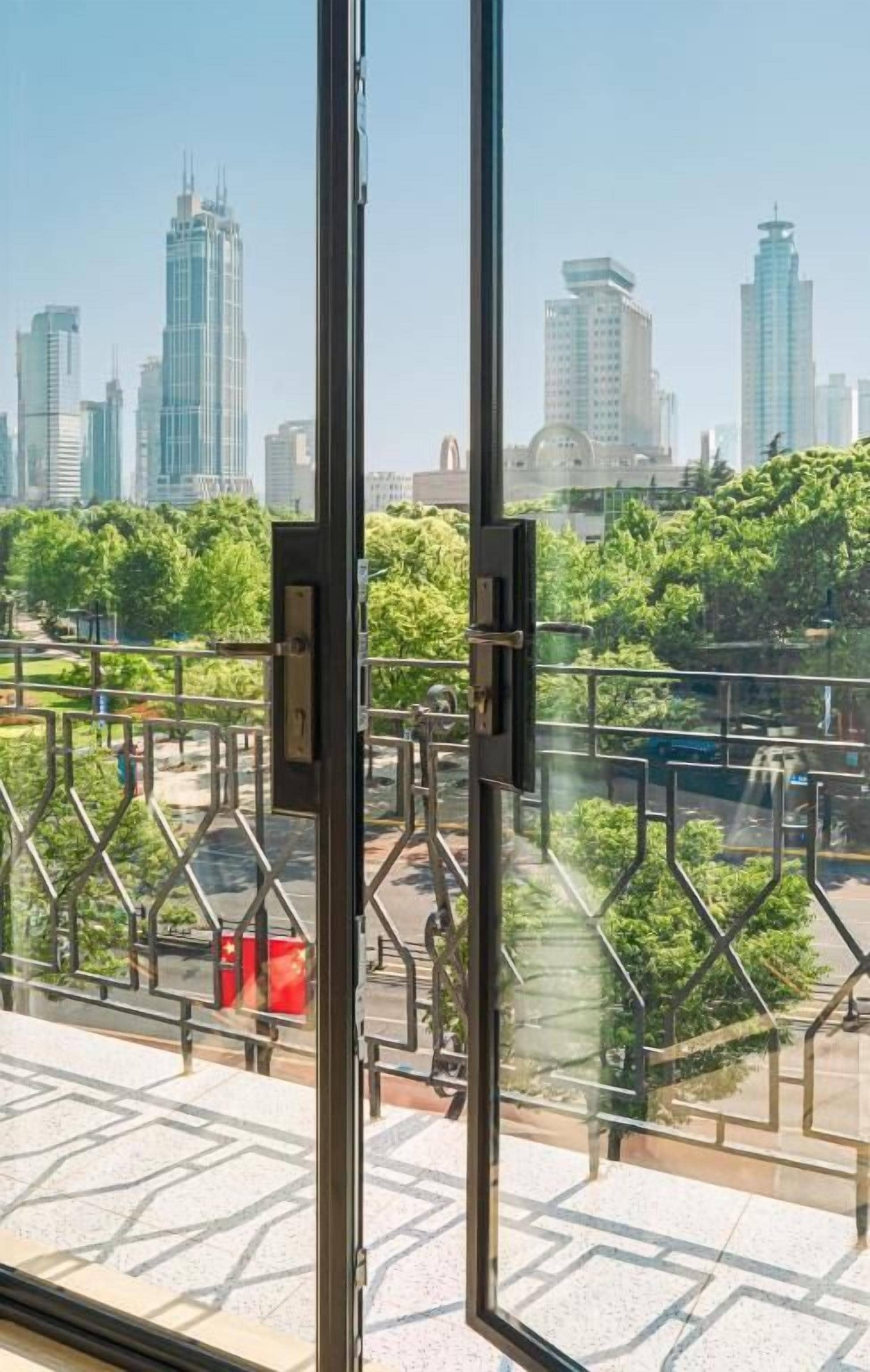 Vista pela janela de um horizonte urbano com edifícios modernos, um parque com árvores e uma passarela para pedestres.