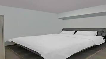 Quarto com cama, paredes brancas e chão escuro.