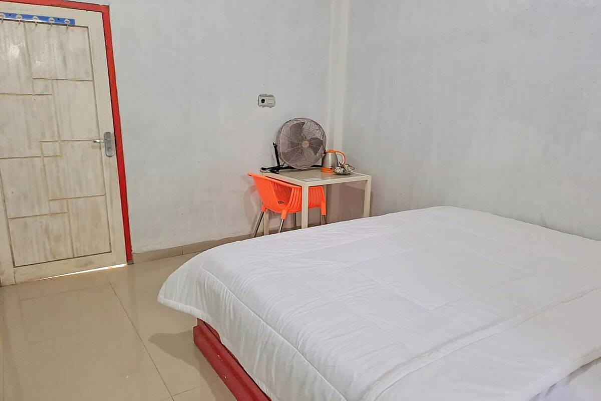 Quarto com cama, escrivaninha, cadeira, ventoinha e porta.