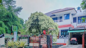 Entrada de um hotel com um portão vermelho, uma placa com o nome Wisma Pakuan e uma árvore ao fundo.