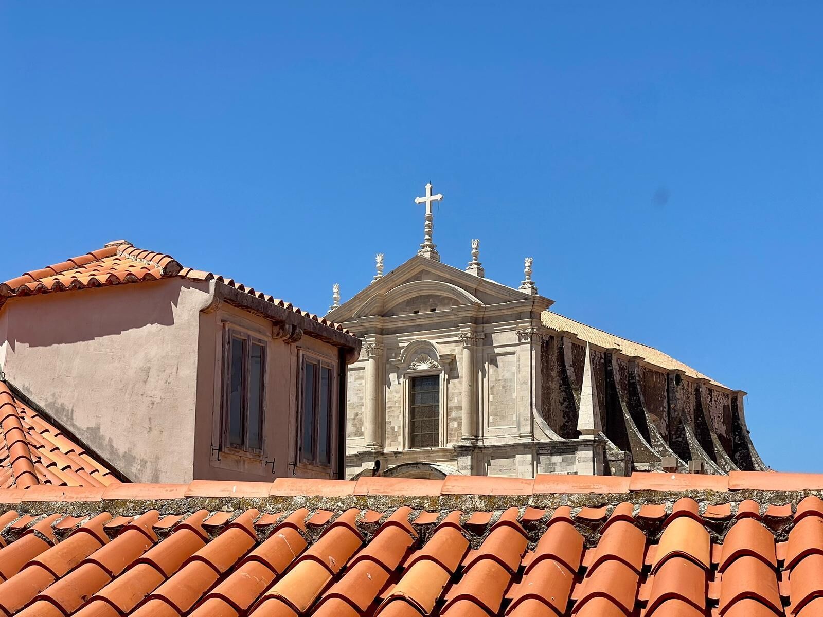Um edifício com cruz no topo, telhado de azulejos e uma janela.