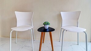 Duas cadeiras brancas com pernas de metal e uma pequena mesa redonda com uma planta em vaso no centro.