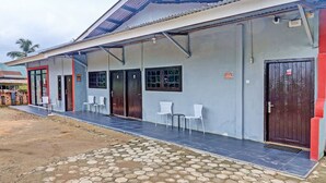 Um edifício com entrada coberta, uma porta com placa e algumas cadeiras na parte externa.