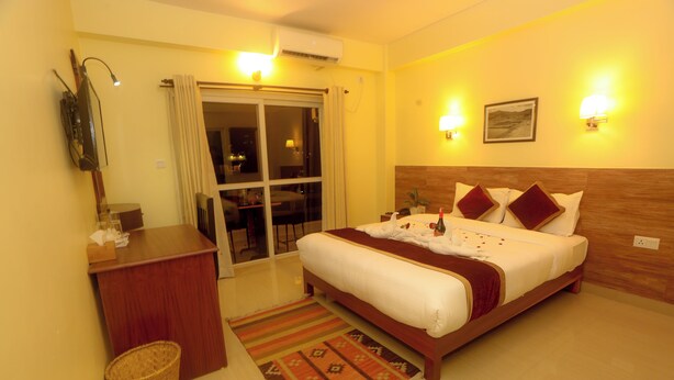 Quarto de hotel com uma cama, mesa de cabeceira, luminária e vista através de uma porta de vidro.