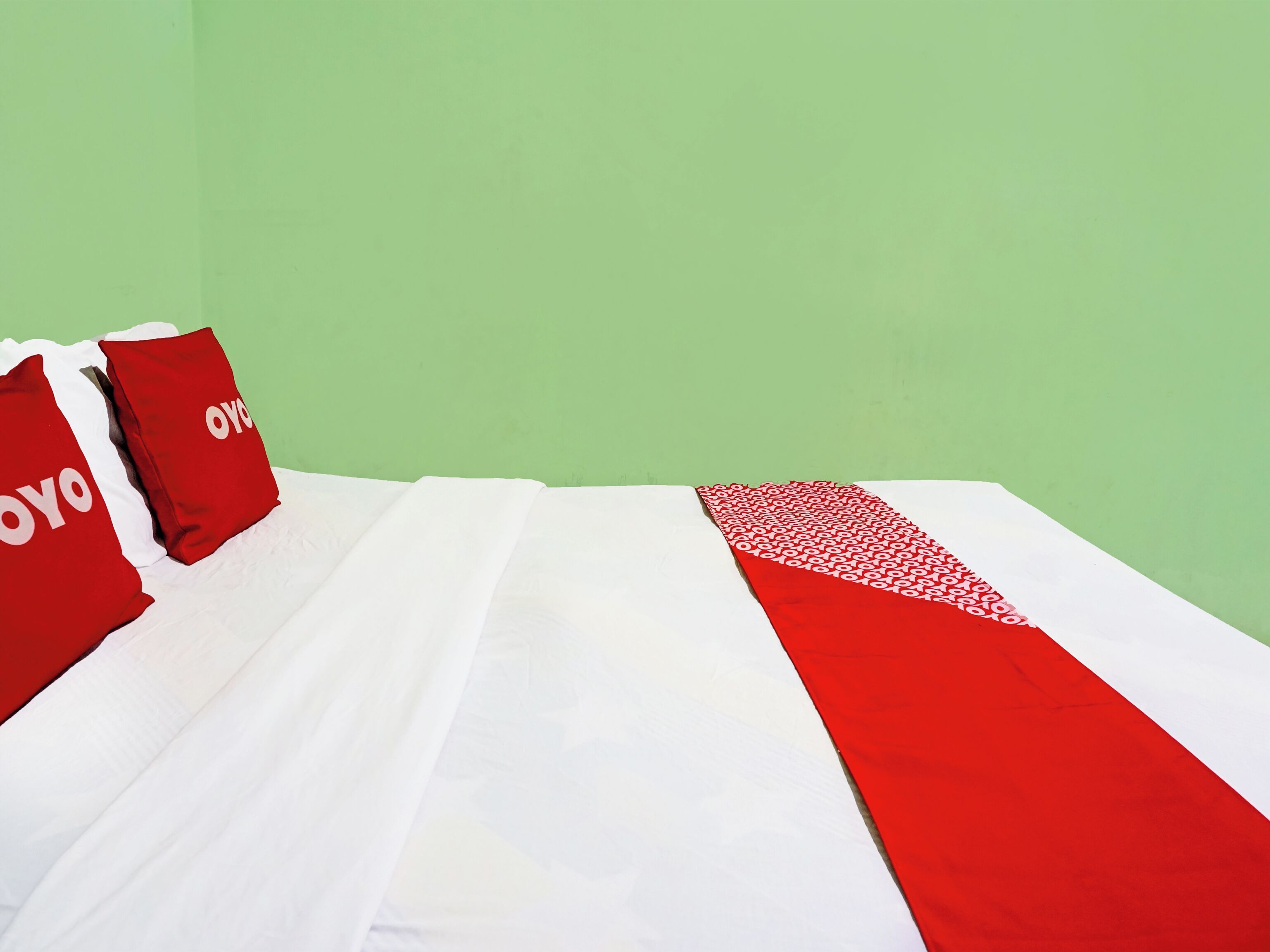 Uma cama com roupa de cama branca e vermelha, dois travesseiros vermelhos com o texto "OYO" e um cobertor estampado em vermelho e branco.