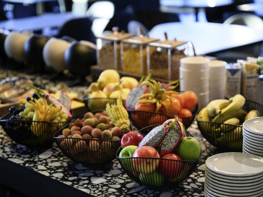 Uma mesa de buffet com diversas frutas e vegetais, incluindo maçãs, bananas e tomates.