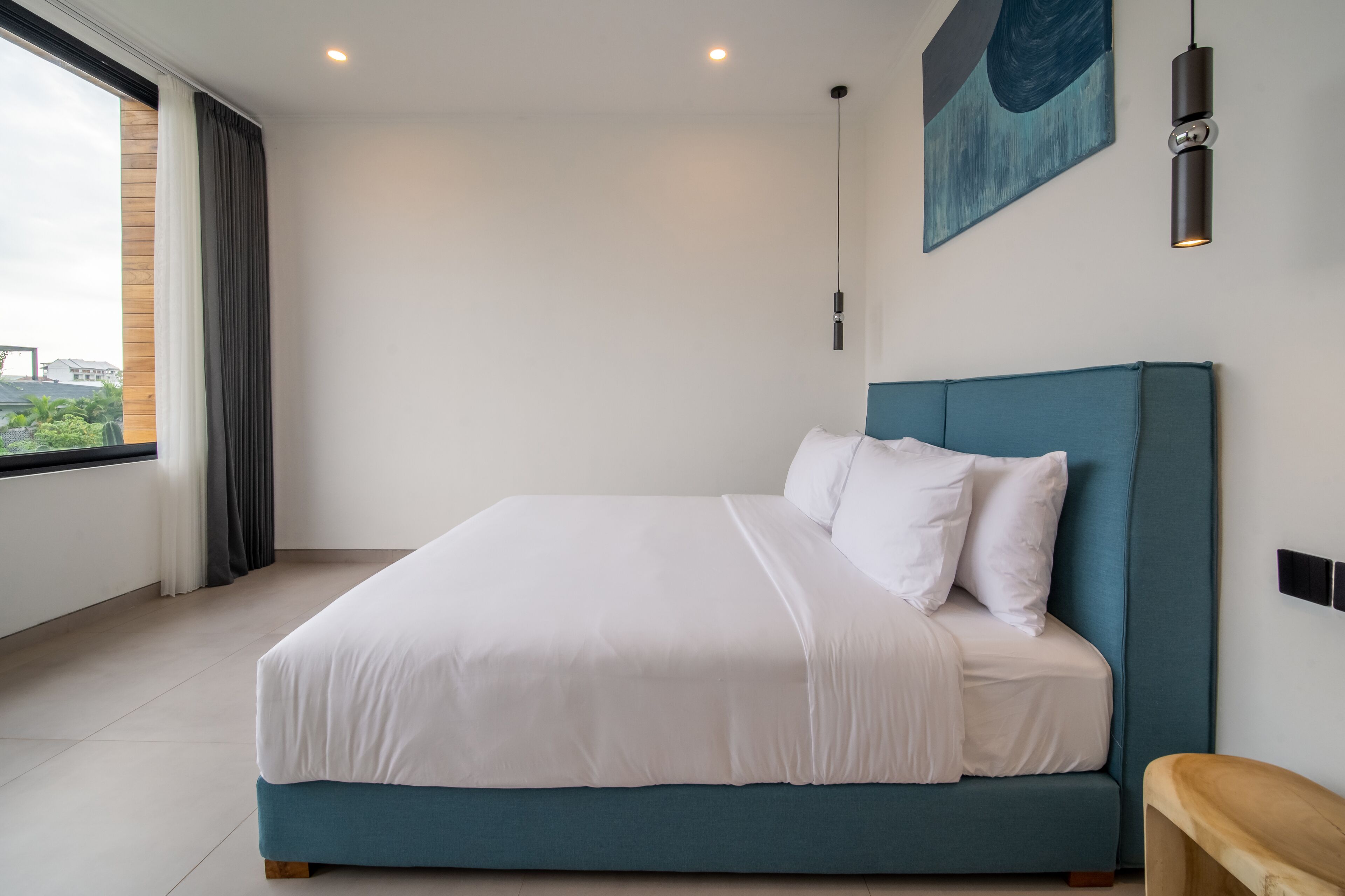 Quarto moderno com uma cama grande, vista para o verde lá fora e um quadro na parede.