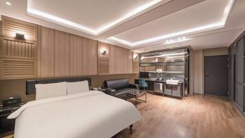 Quarto de hotel moderno com uma cama grande, uma escrivaninha e uma cozinha compacta.