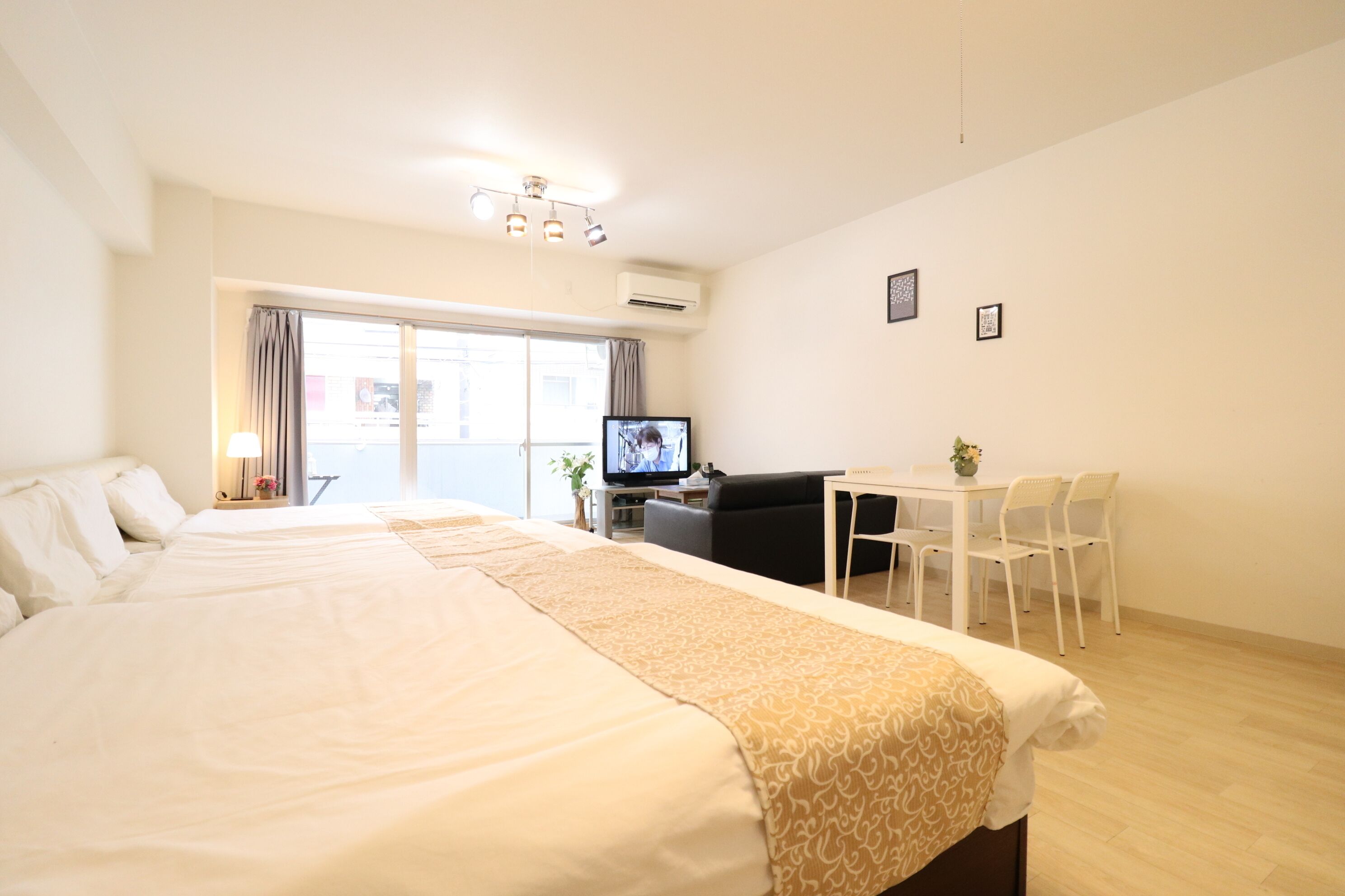 Quarto de hotel com uma cama grande, uma escrivaninha com cadeiras, uma televisão e uma janela com cortinas.
