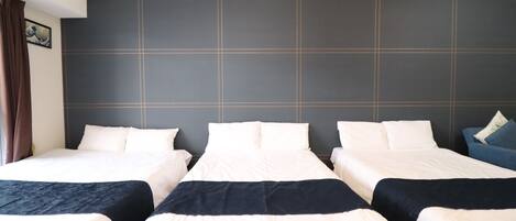 Quarto de hotel com três camas, uma cabeceira escura e uma parede azul decorativa.