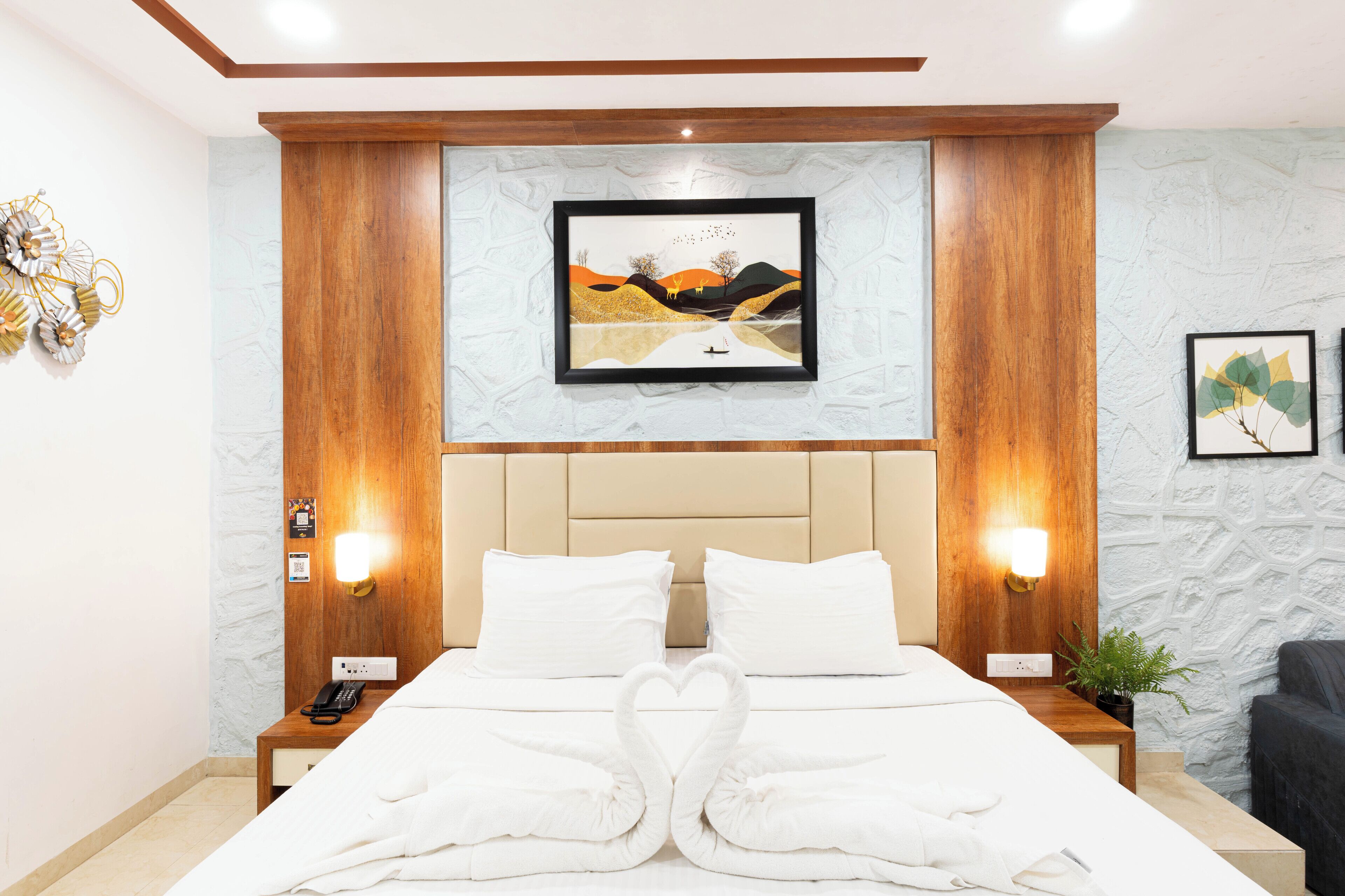 Quarto de hotel com uma cama grande, cabeceira de madeira, duas mesas de cabeceira com abajures, uma obra de arte emoldurada acima da cama e um telefone fixado na parede.
