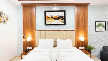 Quarto de hotel com uma cama grande, cabeceira de madeira, duas mesas de cabeceira com abajures, uma obra de arte emoldurada acima da cama e um telefone fixado na parede.