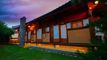 Uma casa de madeira tradicional com chaminé de pedra, varanda de madeira e gramado bem cuidado.