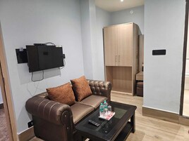 Sala de estar com sofá de couro, televisão de tela plana na parede, móvel de madeira e mesa de centro com controle remoto e garrafas.