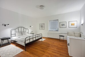 Quarto com cama, mesa de cabeceira, luminária, radiador, janela e uma obra de arte na parede.