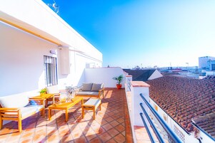 Terraço no telhado com um edifício branco, piso de azulejos, mobiliário de exterior e vista para a paisagem urbana.