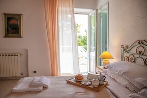 Quarto de hotel com cama, bandeja de café da manhã, janela com cortinas, radiador e um quadro na parede.