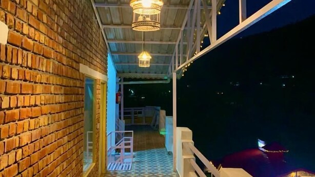 Uma galeria coberta com uma parede de tijolos de um lado e um corrimão do outro, que conduz a uma varanda com vista para o céu noturno.