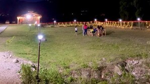 Uma área externa gramada com uma pequena estrutura iluminada e luzes de cordão.