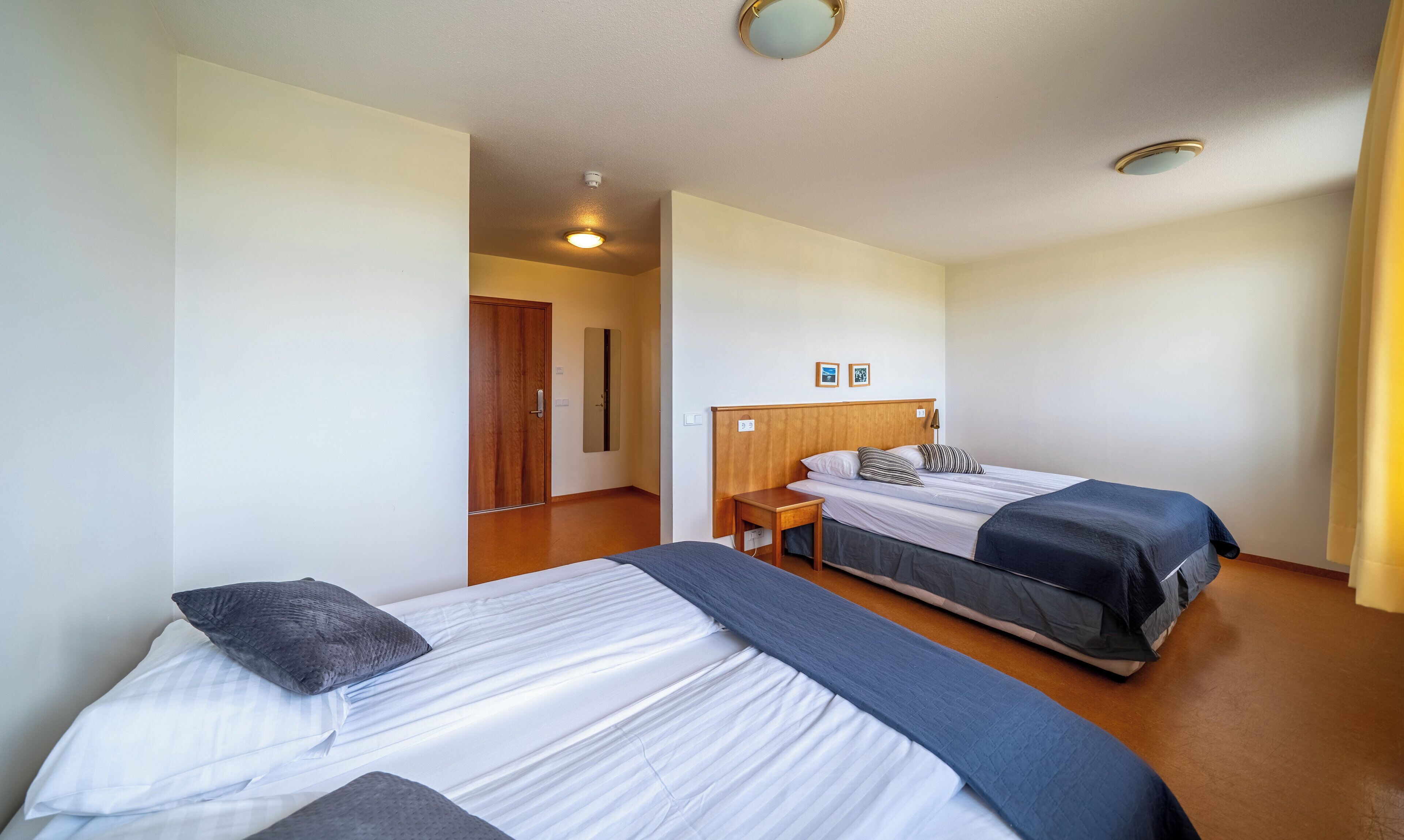 Quarto de hotel com duas camas, cabeceira de madeira, mesa de cabeceira e espelho na parede.