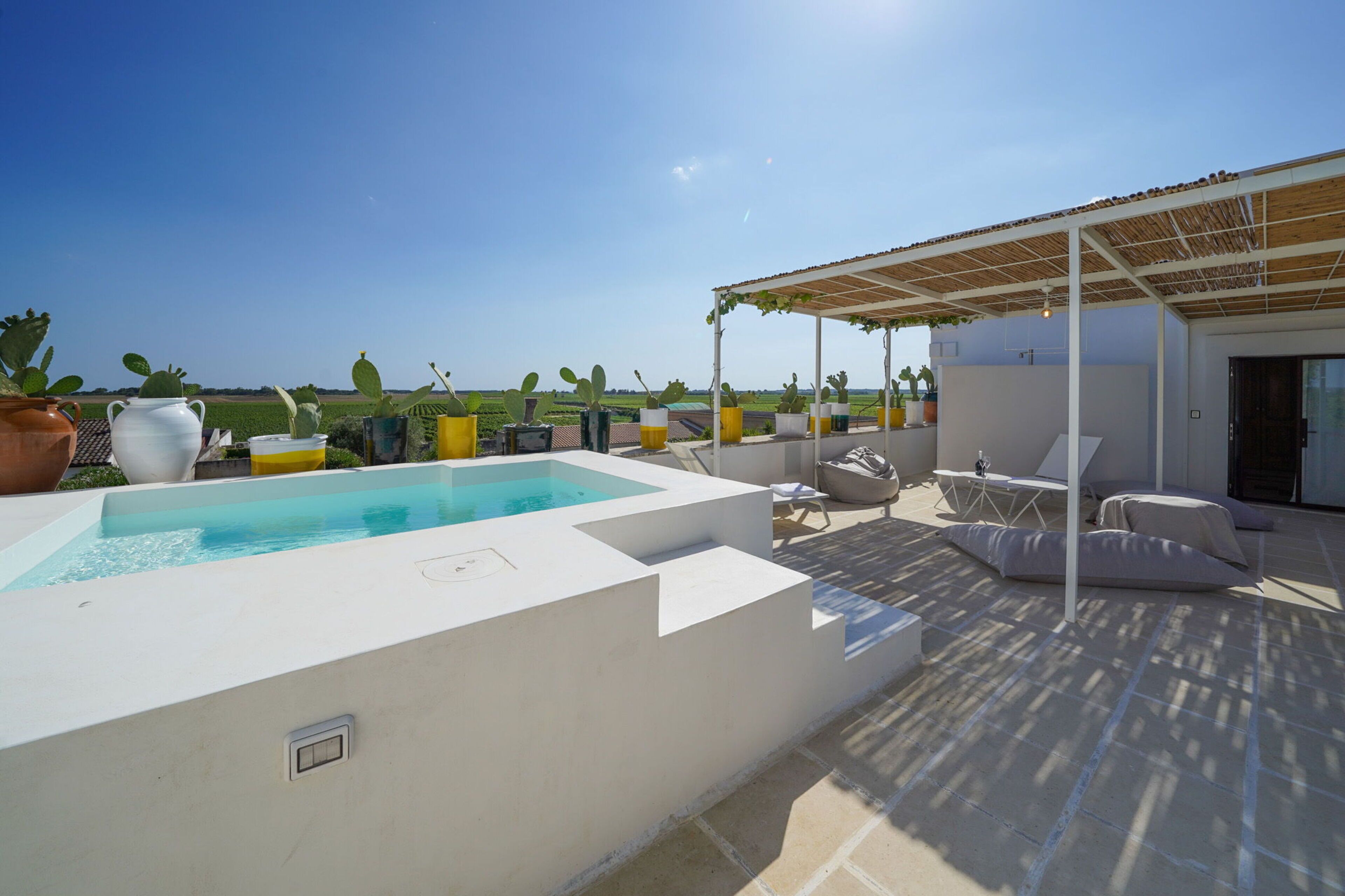 Área de piscina no terraço com pérgola, mobiliário externo e cactos ao fundo.