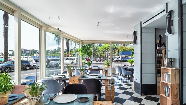 Restaurante com mesas ao ar livre, chão xadrez e vista para a rua.