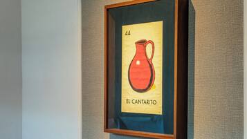 Obra de arte emoldurada de um jarro vermelho com a etiqueta "EL CANTARITO" em uma parede texturizada.