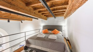 Quarto com uma cama, duas almofadas laranjas, cabeceira e chão xadrez.