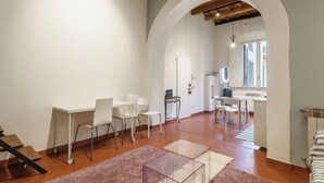 Uma sala de estar moderna com área de jantar, móveis brancos e cozinha ao fundo.