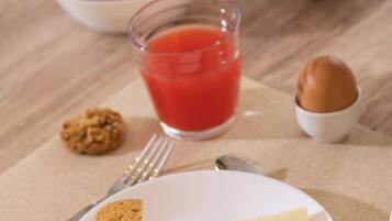 Uma mesa de café da manhã com um prato de comida, incluindo torradas, queijo e patê, um copo de suco vermelho e uma tigela de cerejas.