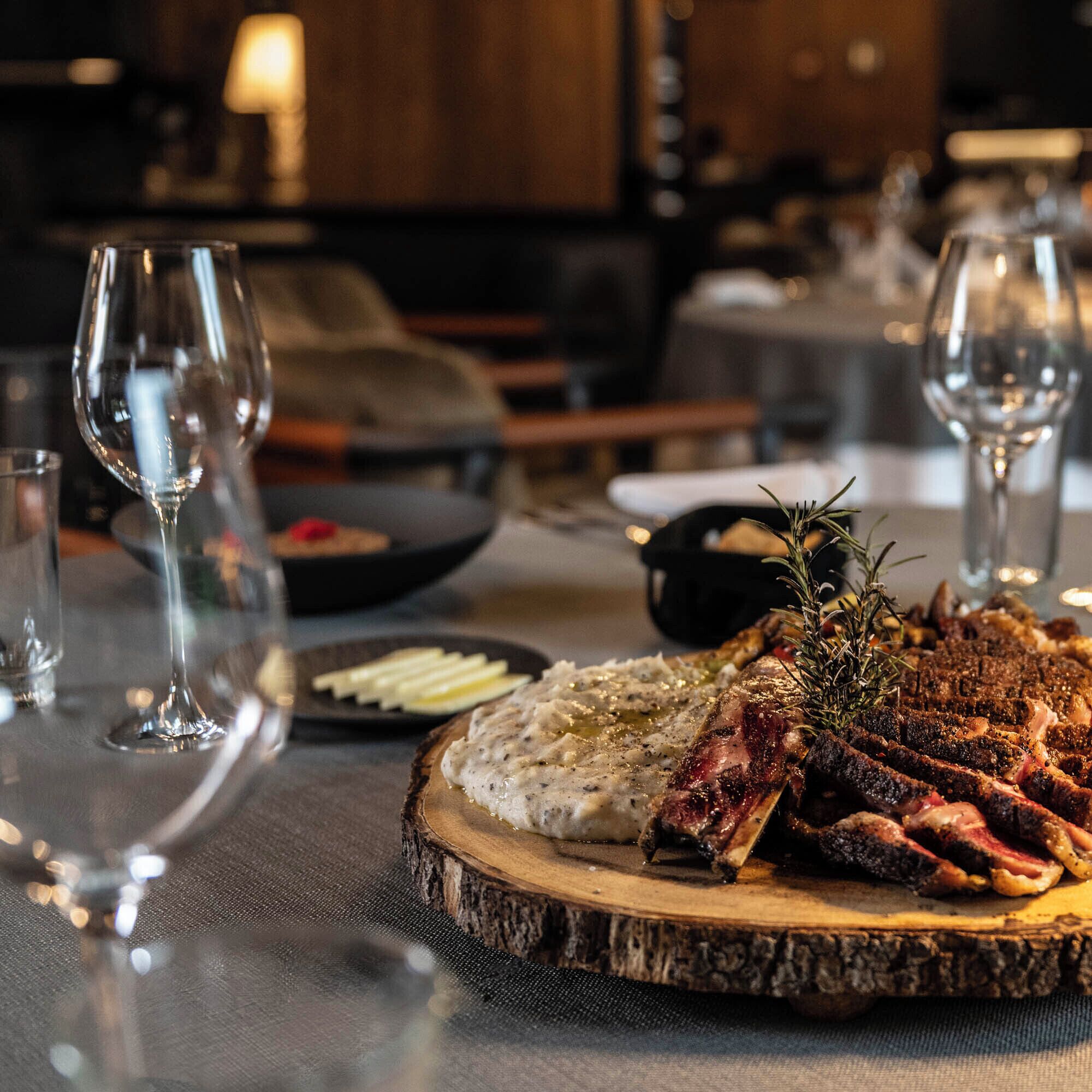 Uma mesa de jantar com um prato de carne assada, um bowl de purê de batata e um ramo de alecrim.