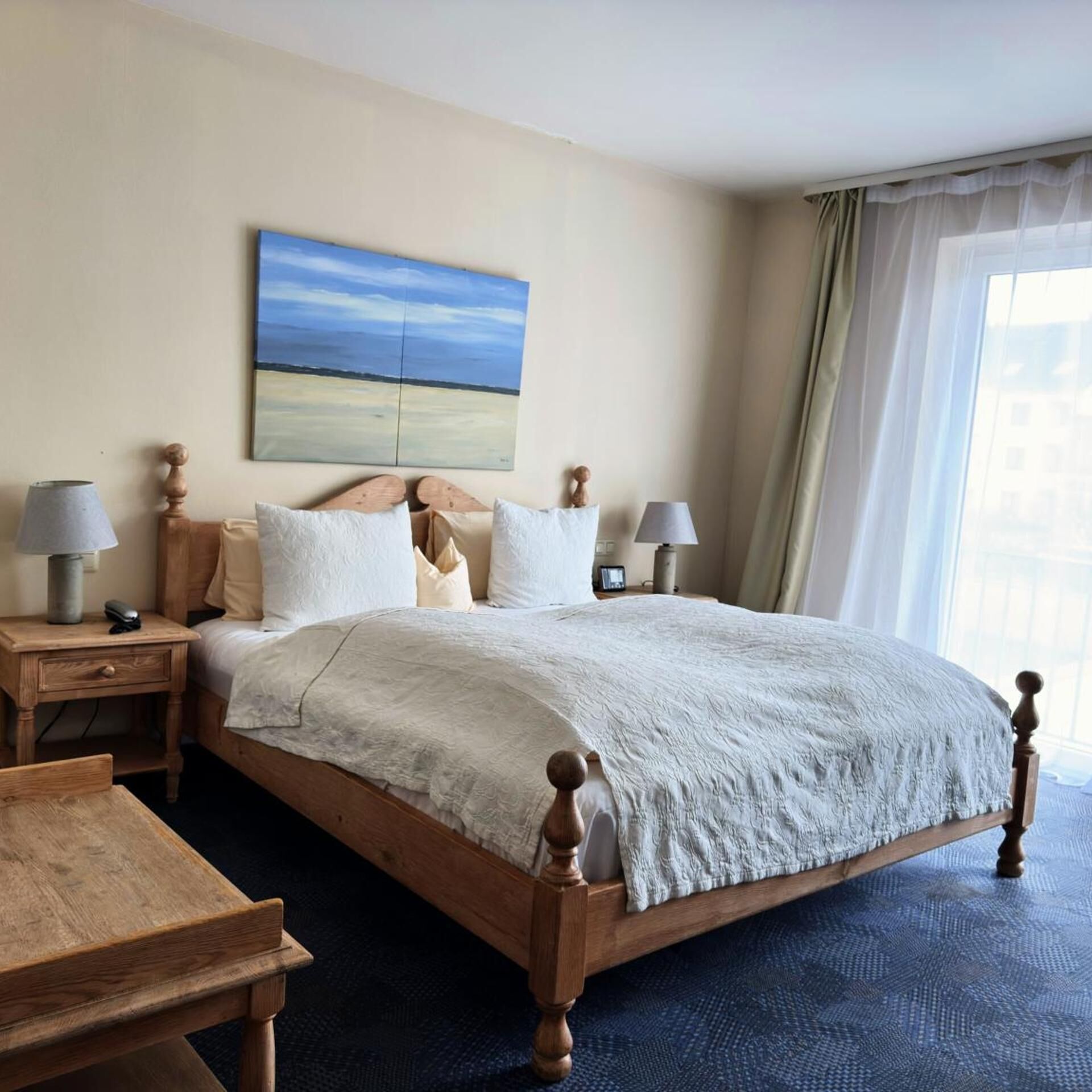 Quarto de hotel com uma cama grande, duas mesas de cabeceira, uma escrivaninha e um quadro na parede.