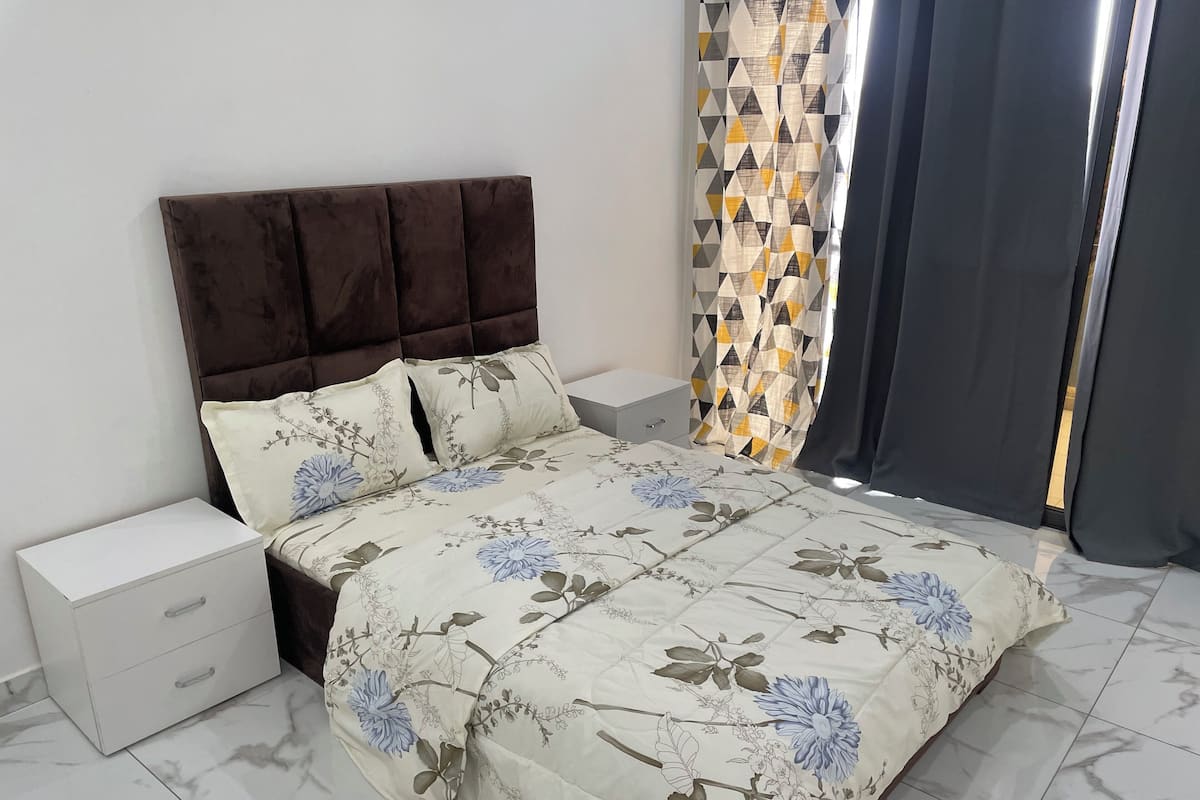 Quarto com cama, mesas de cabeceira e janela com cortinas.
