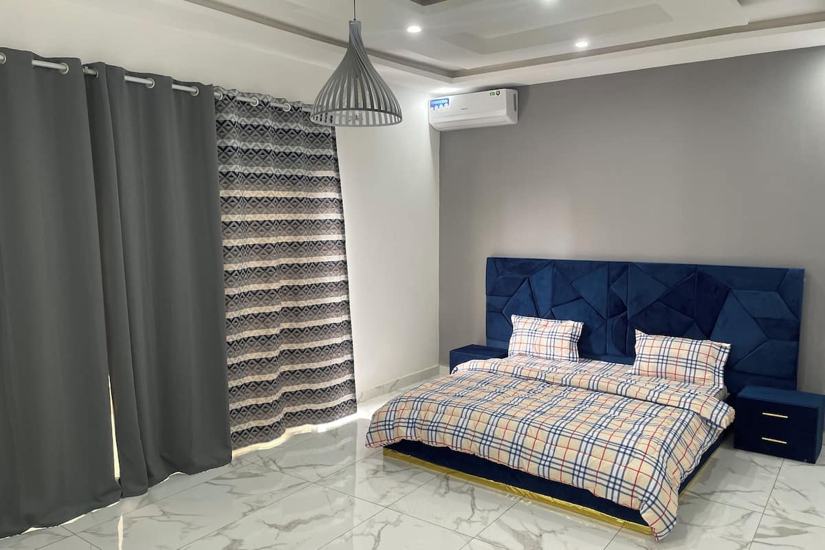 Quarto moderno com cama, mesas de cabeceira, luminária pendente e aparelho de ar condicionado.