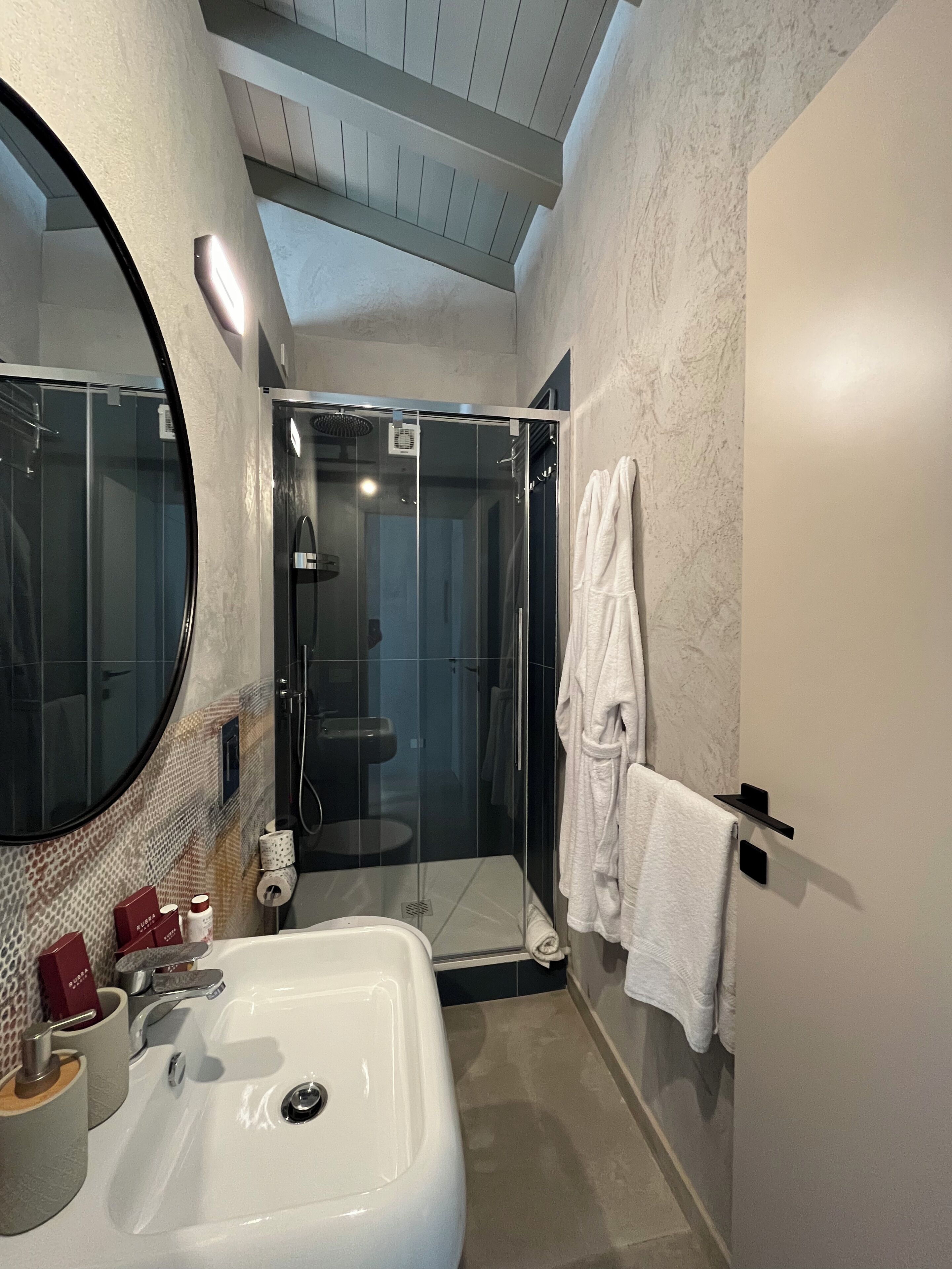 Uma casa de banho moderna com um espelho grande, uma sanita branca, um chuveiro com parede de vidro e um porta-toalhas.