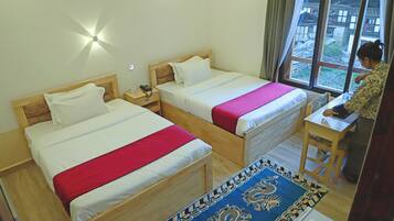 Quarto de hotel com duas camas, uma escrivaninha, uma cadeira, um tapete estampado e vista para o exterior.