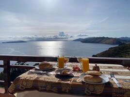 Mesa posta com itens de café da manhã e vista panorâmica de um lago e montanhas.
