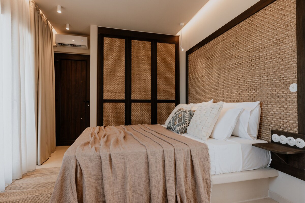 Quarto com cama, ar-condicionado fixado na parede, porta de madeira e parede texturizada.