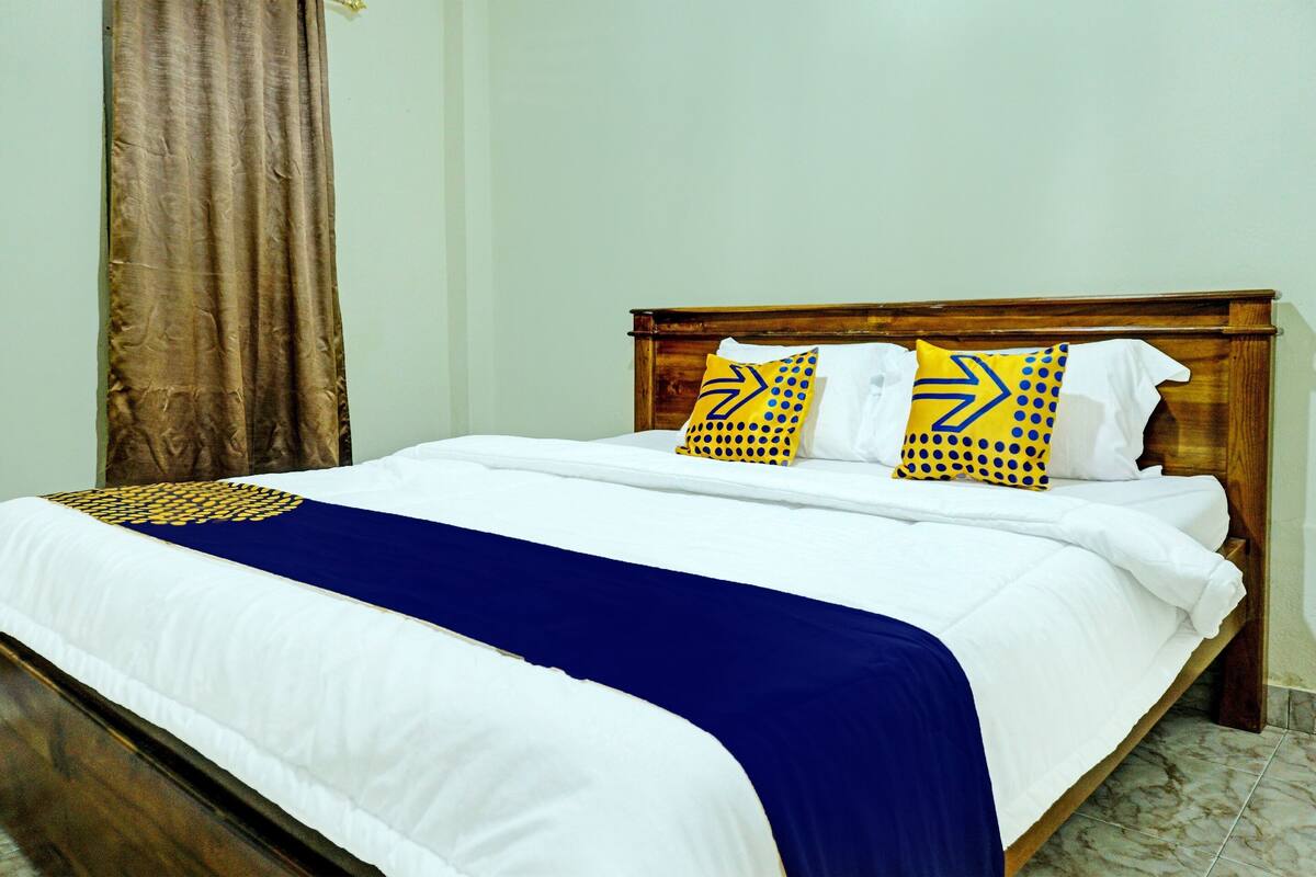 Uma cama bem arrumada com roupa de cama branca e azul, dois travesseiros com estampas amarelas e azuis e uma cabeceira de madeira.