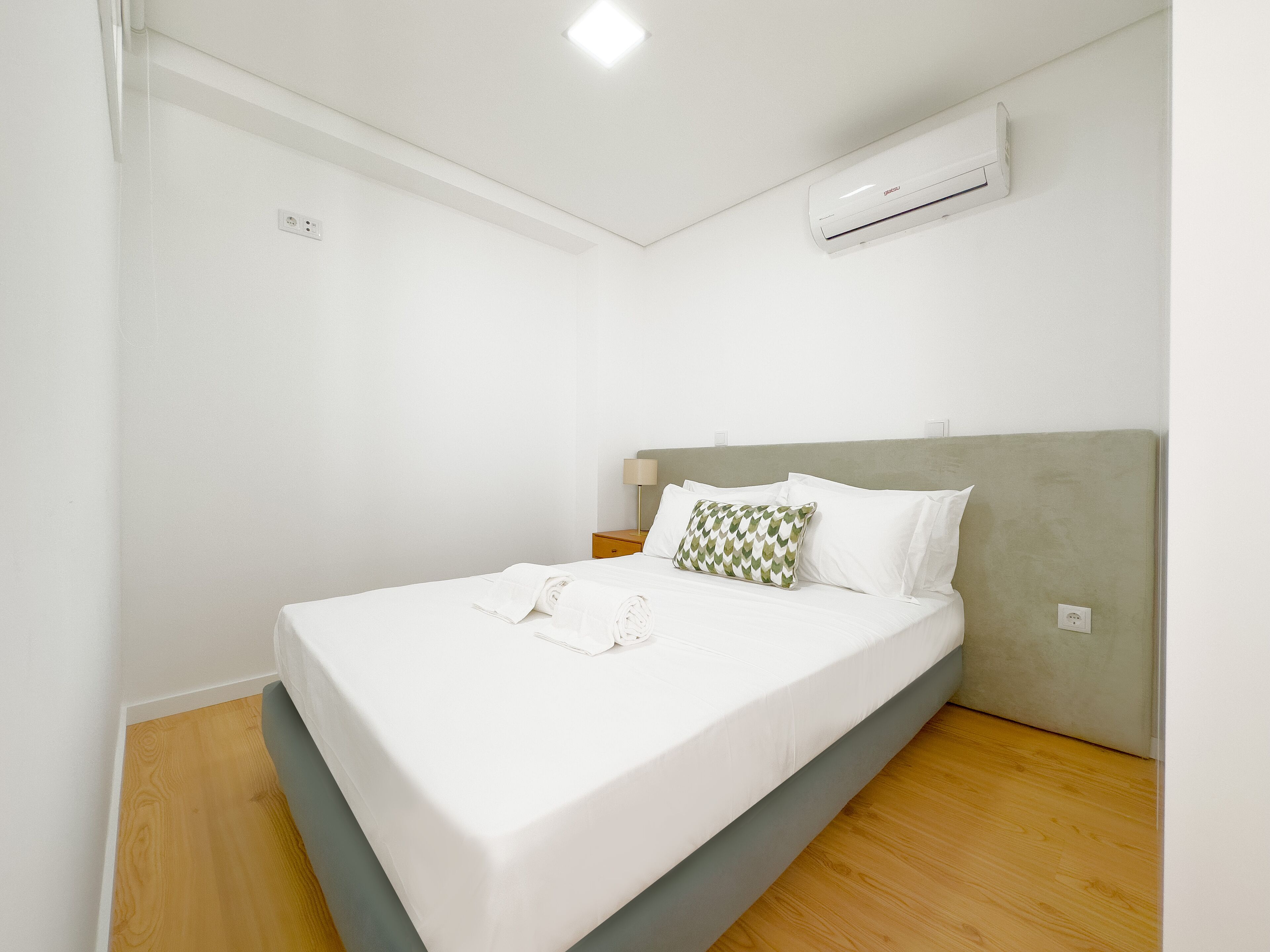 Um quarto moderno e limpo, com cama, almofadas e ar condicionado.