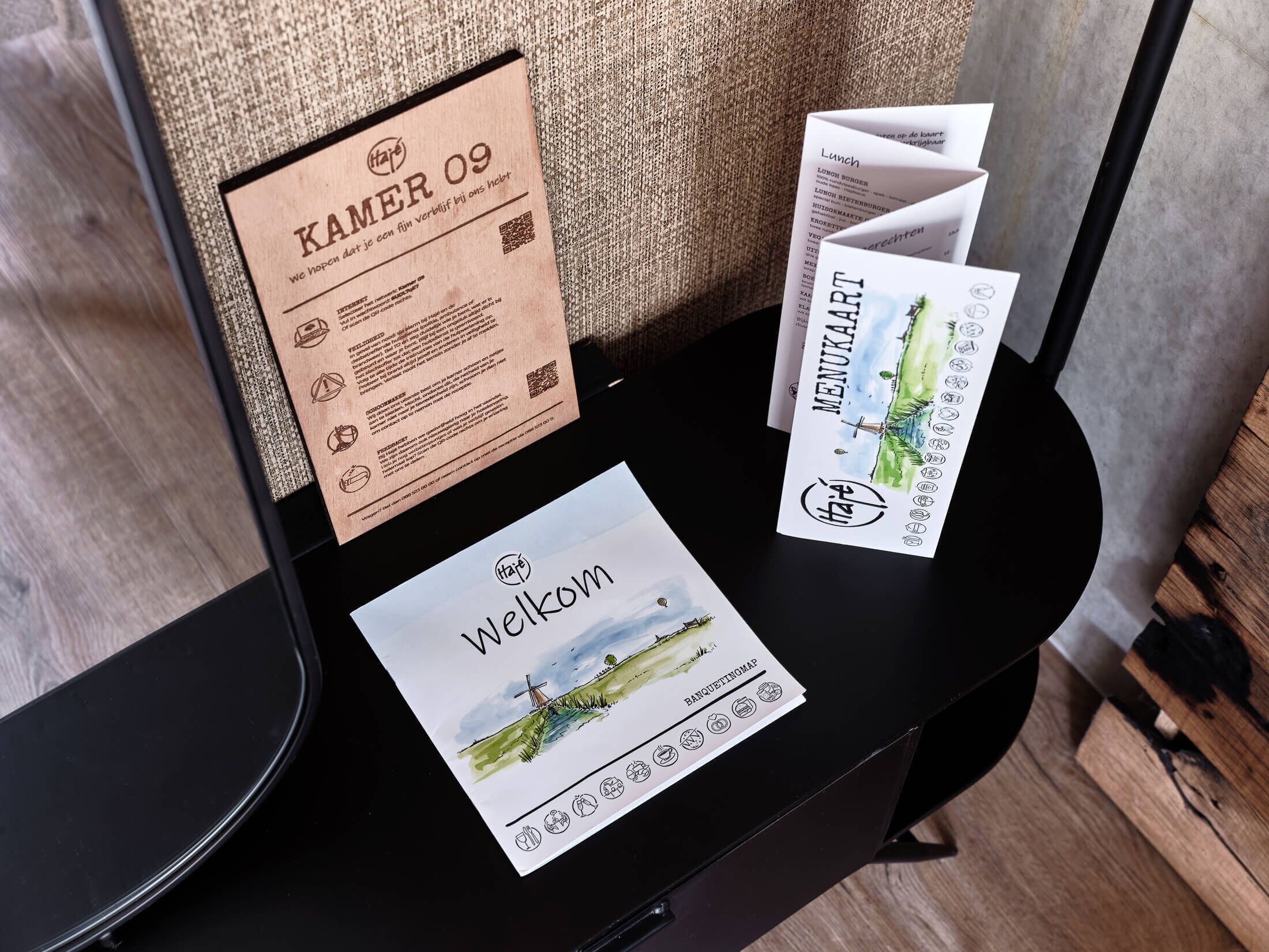 Uma mesa preta com um menu, um cartão de boas-vindas e um cartão com uma ilustração de paisagem.