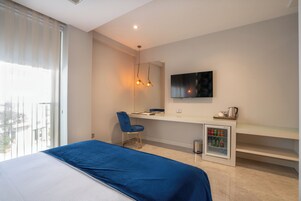 Quarto de hotel moderno com uma cama grande, uma escrivaninha, uma cadeira, uma televisão na parede e um mini-refrigerador.