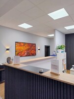 Uma área de recepção de hotel com design moderno, com um balcão de recepção, uma grande pintura abstrata na parede e uma planta em vaso.