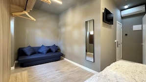 Um quarto moderno com um sofá azul escuro, um espelho grande, uma televisão de tela plana e um tapete branco e macio.