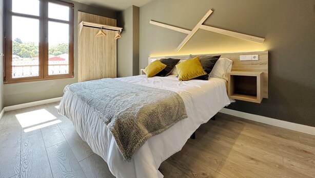 Quarto moderno com uma cama grande, cabeceira de madeira e vista para o exterior através de uma janela.