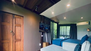 Quarto com guarda-roupa de madeira, cama com roupa de cama azul, sofá branco e televisão na parede.