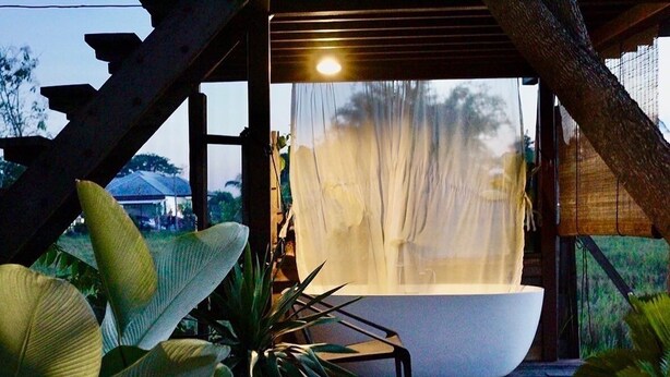 Uma banheira de hidromassagem sob uma pérgola de madeira, com vista para uma área com tendas ao fundo.